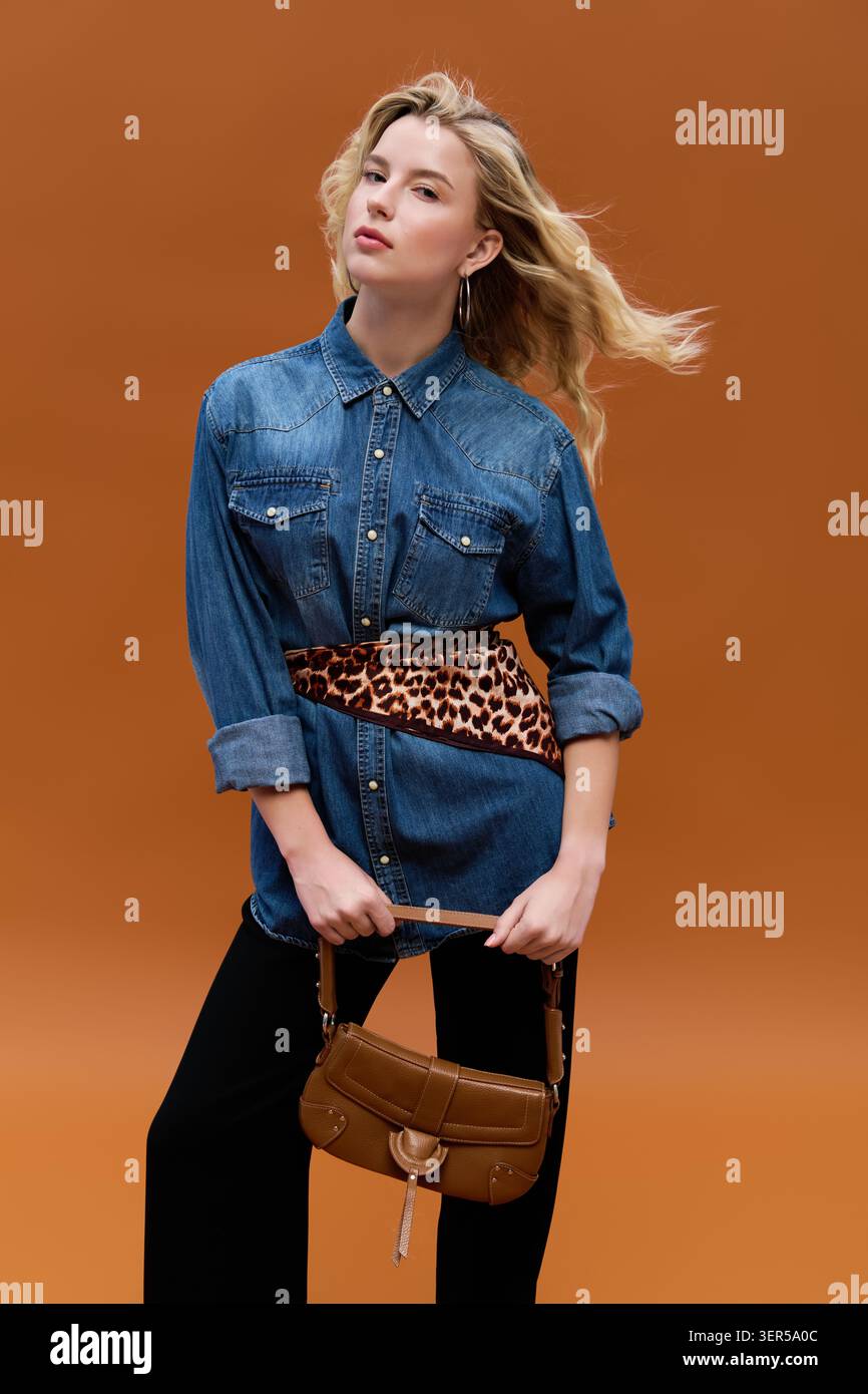 Blonde woman displays her trendy denim look and handbag in studio Stock ...