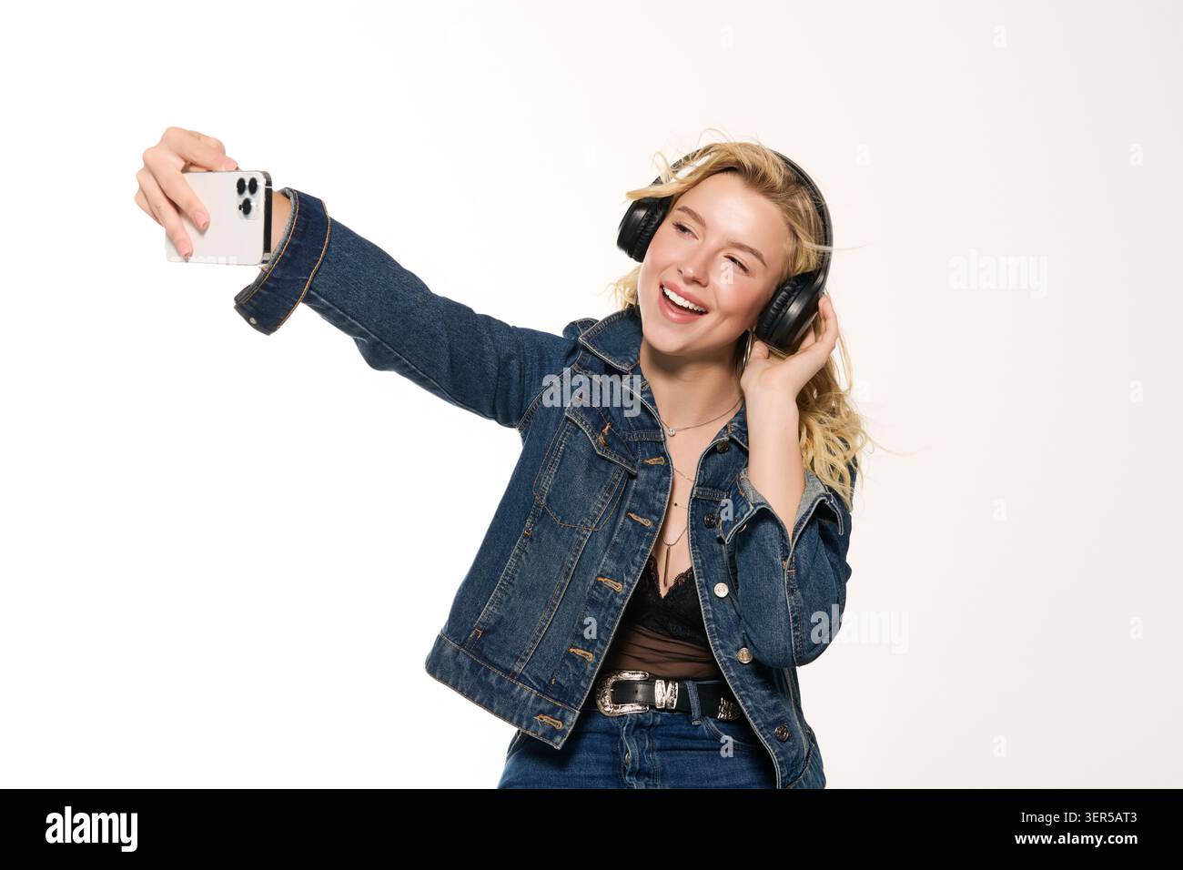 Cheerful blonde woman in denim and headphones enjoys a casual moment ...