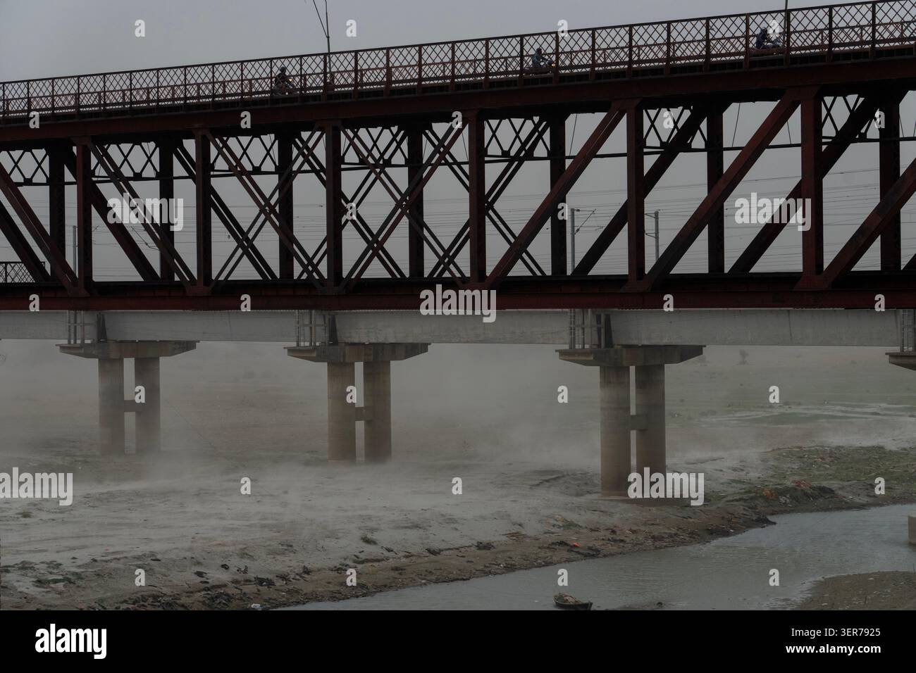 Vehicles move through a railway bridge over river Ganges while dusty ...