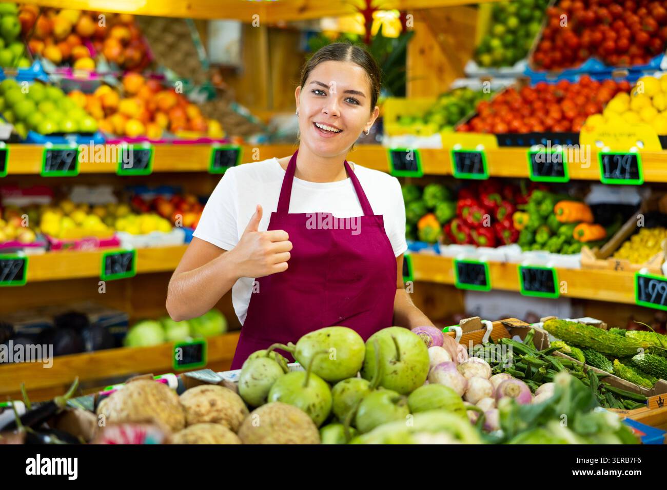 Portrait of happy woman in apron selling organic zucchini in shop Stock ...