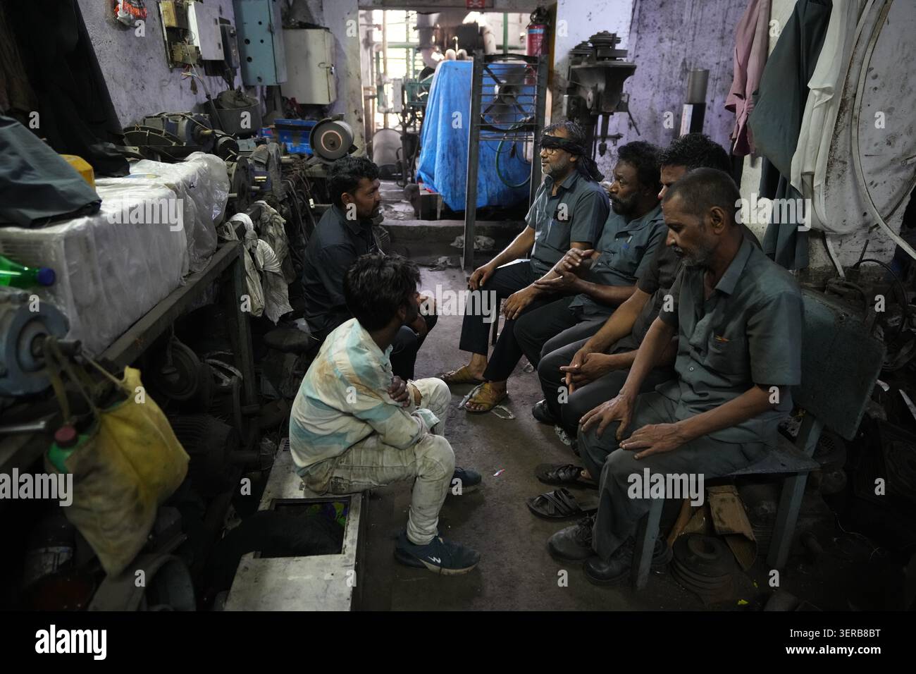 Workers sit near a fan during a break on a hot day at a textile factory ...