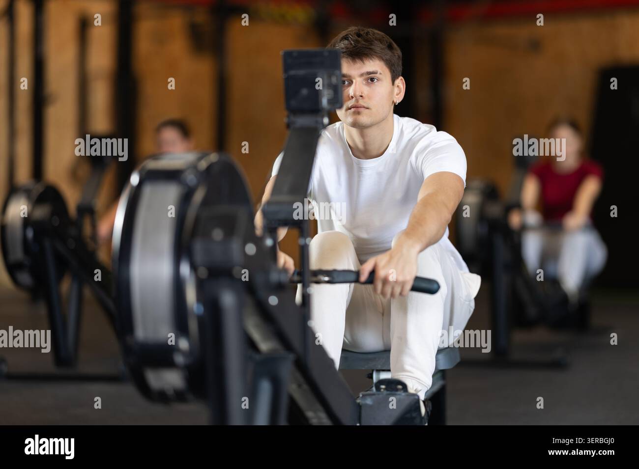 Focused guy works out with rowing machine during class at fitness club ...