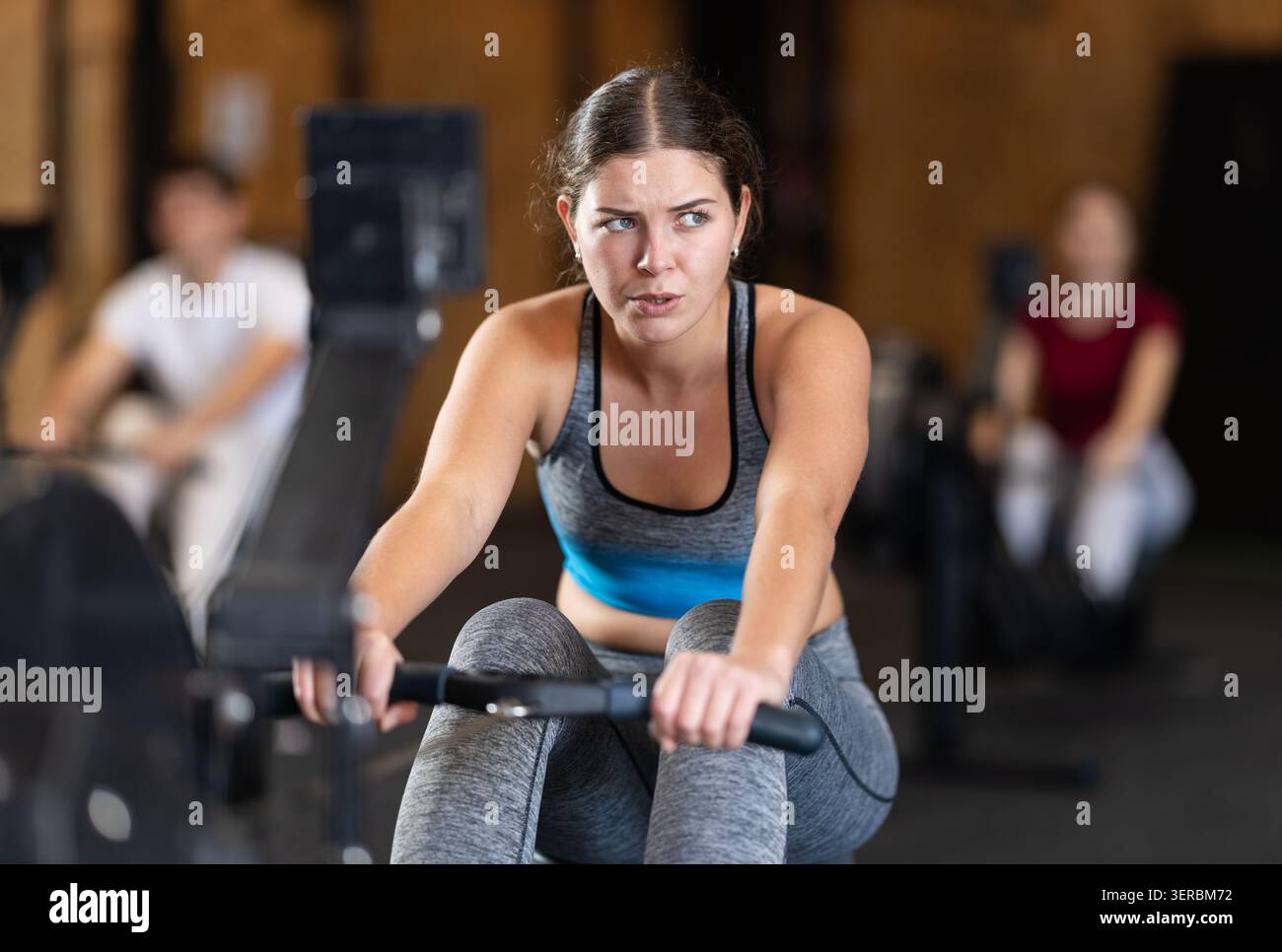 Focused girl works out with rowing machine during class at fitness club ...