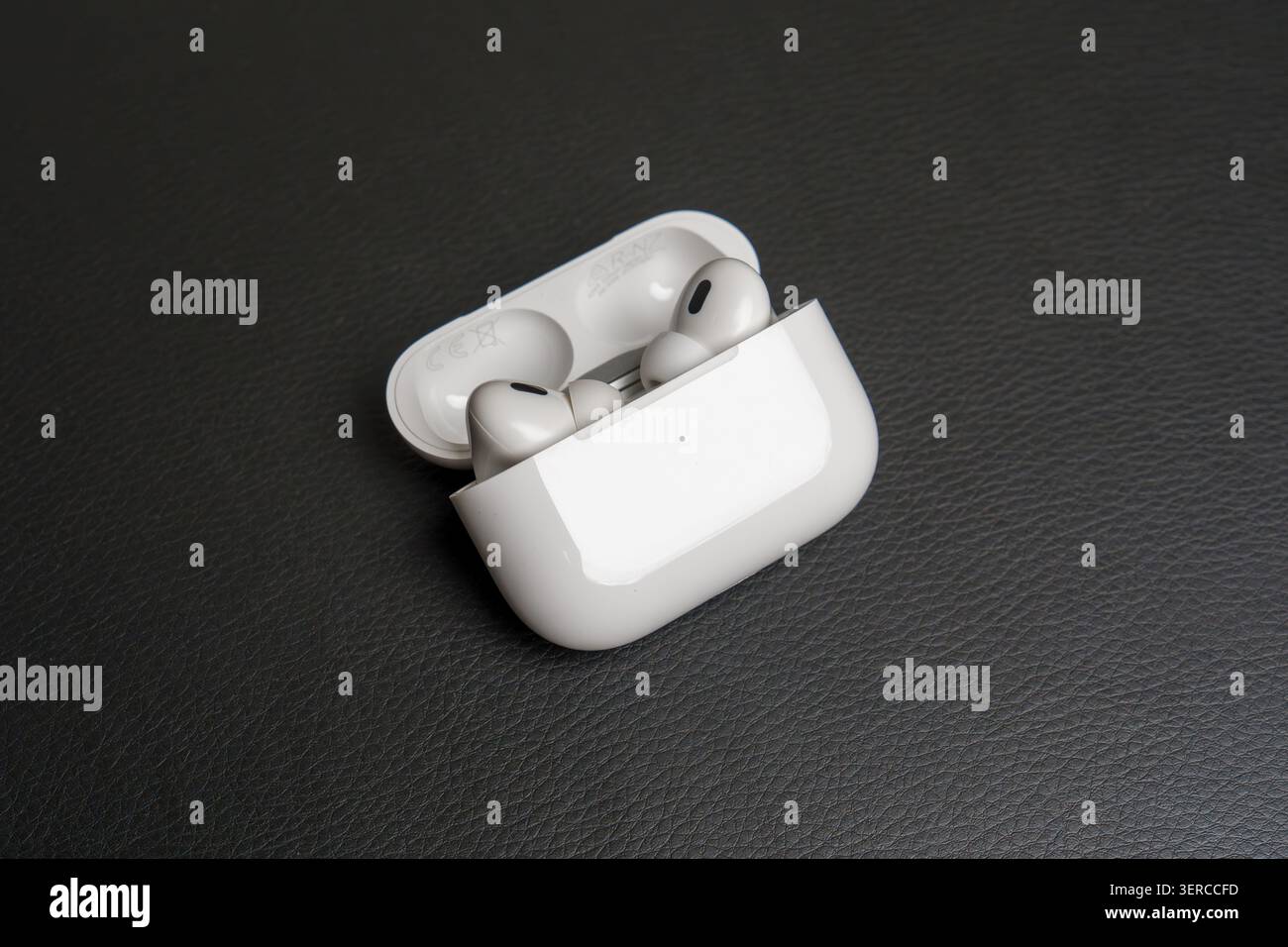 White earbuds rest in open charging case. Case sits on dark textured ...