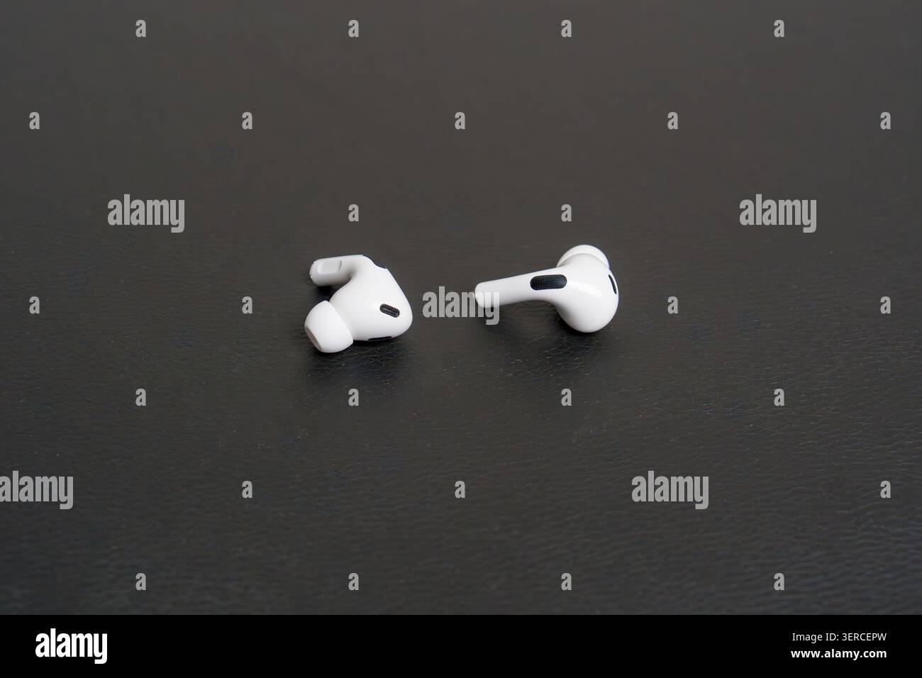White wireless earbuds rest on dark textured surface. Minimalist shot ...