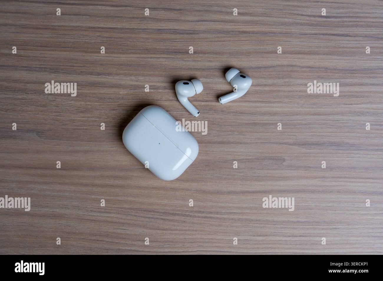 White earbuds rest beside their case on wood grain surface. Minimalist ...
