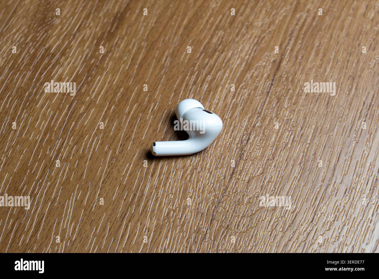 Single white earbud rests on wooden surface. Minimalist composition ...