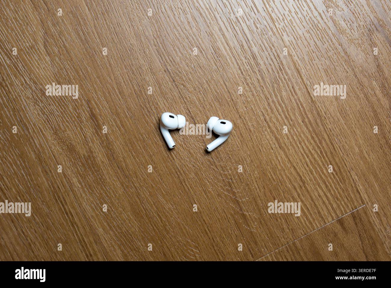 White earbuds lie on a wooden surface. Sleek design rests on warm-toned ...