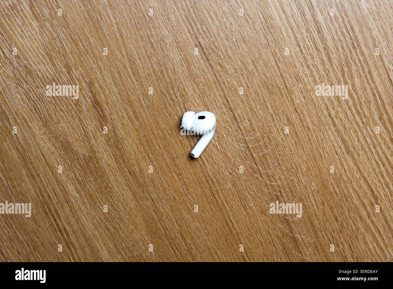 Single white earbud rests on wooden surface. Earbud lies flat, slightly ...