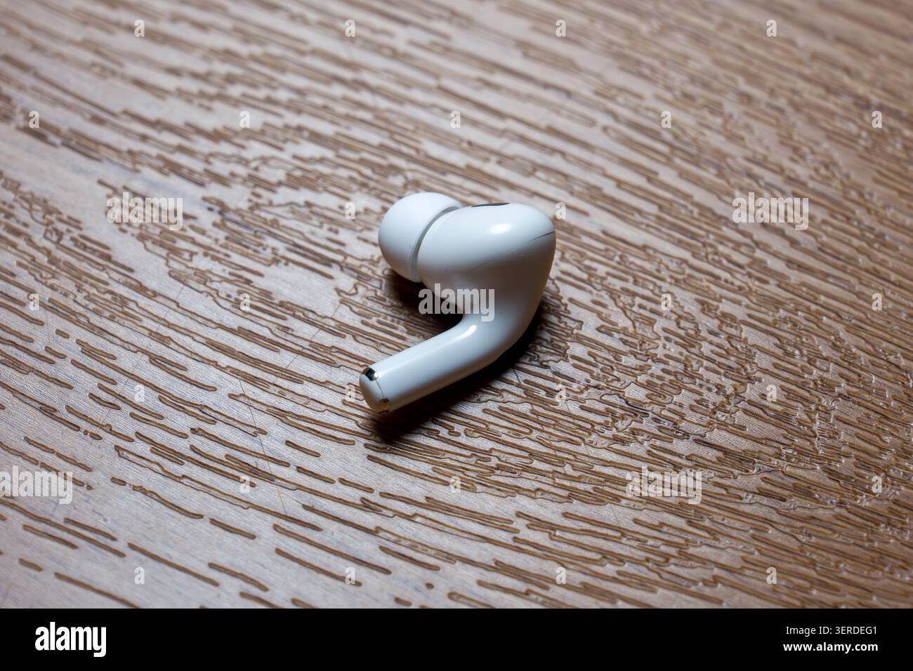 Single white earbud rests on wood grain surface. Simple, clean ...