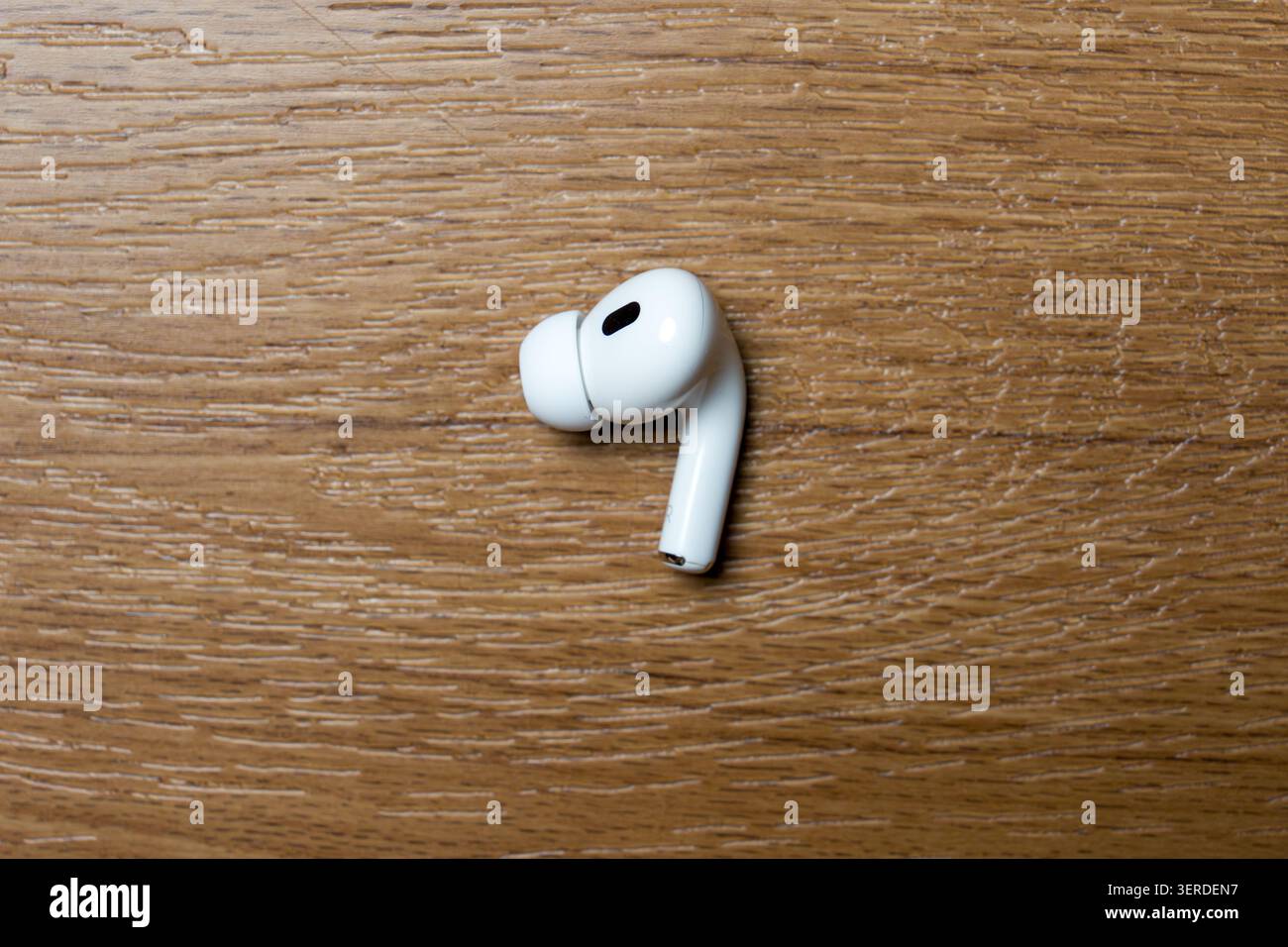 Single white earbud rests on wooden surface. Minimalist view highlights ...