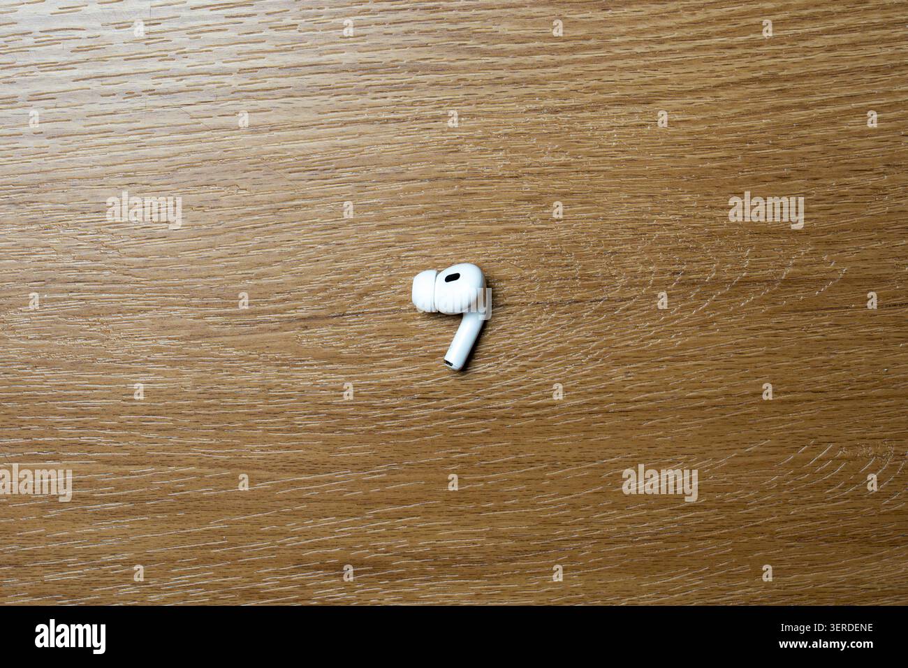 Single white wireless earbud rests on wooden surface. Earbud positioned ...