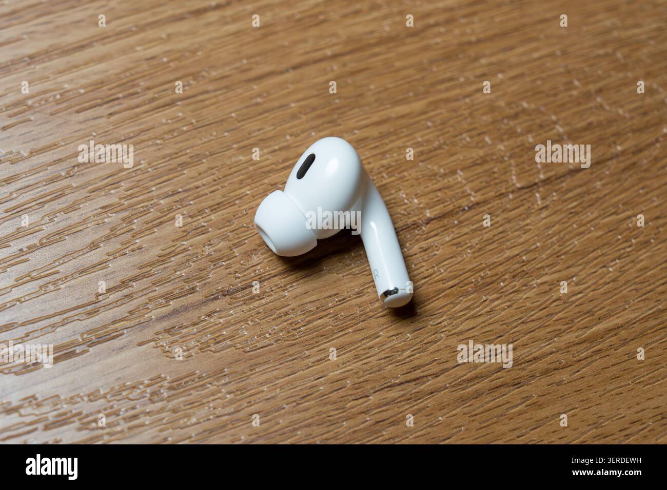 Single white earbud rests on wooden surface. Earbud lies flat, facing ...