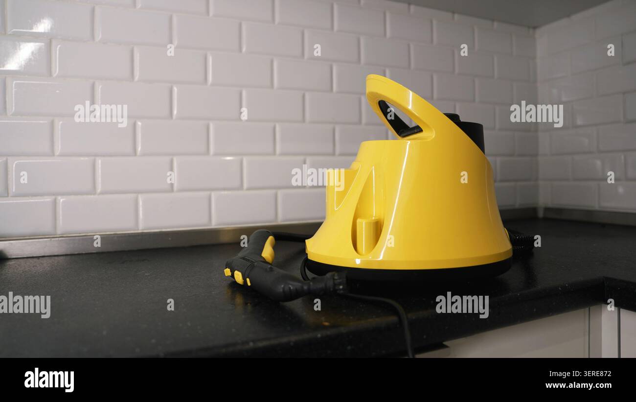 Yellow steam cleaner sits on black kitchen countertop with white tile ...