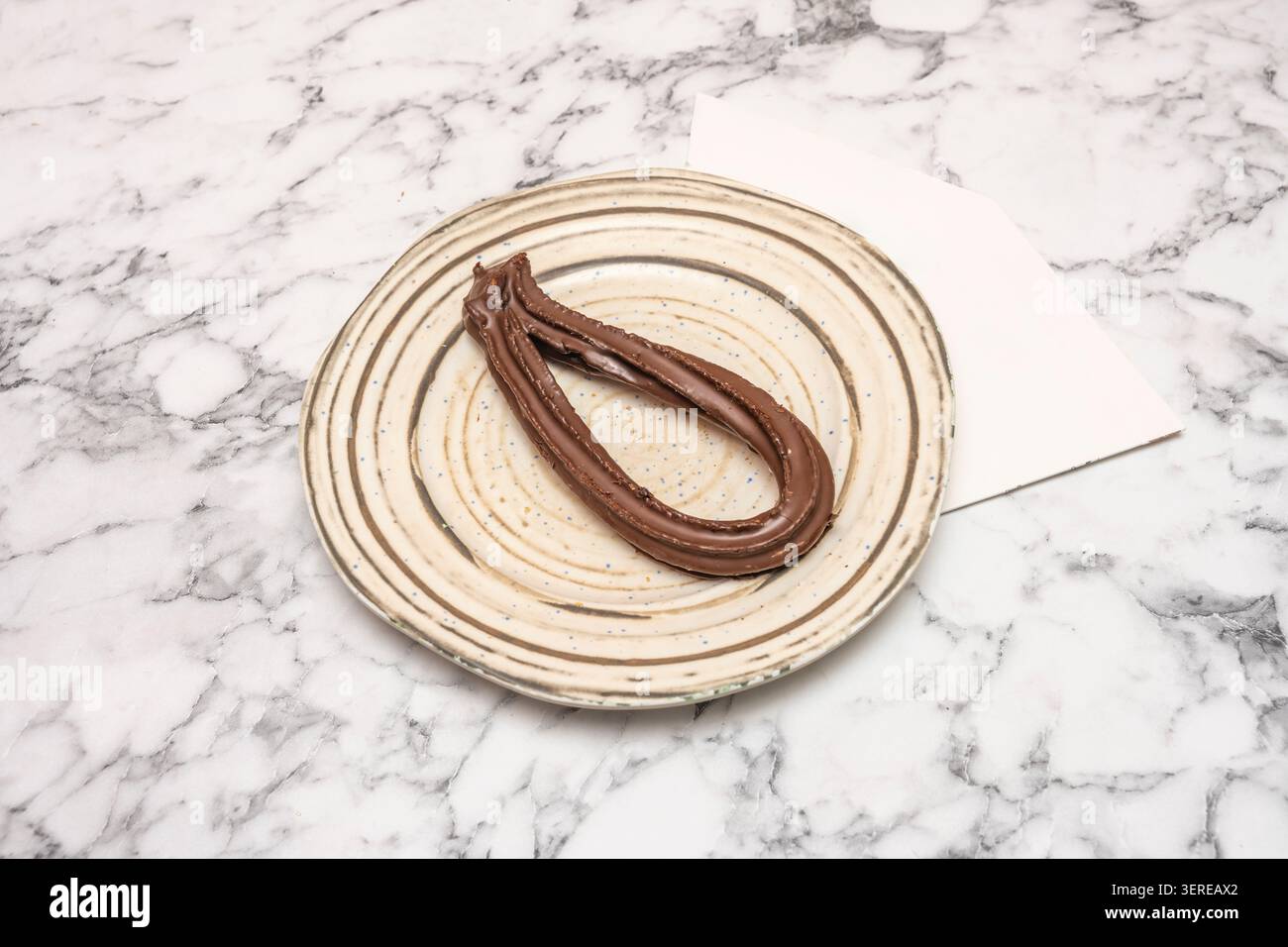 A chocolate-glazed churro sits centered on a ceramic plate with brown ...