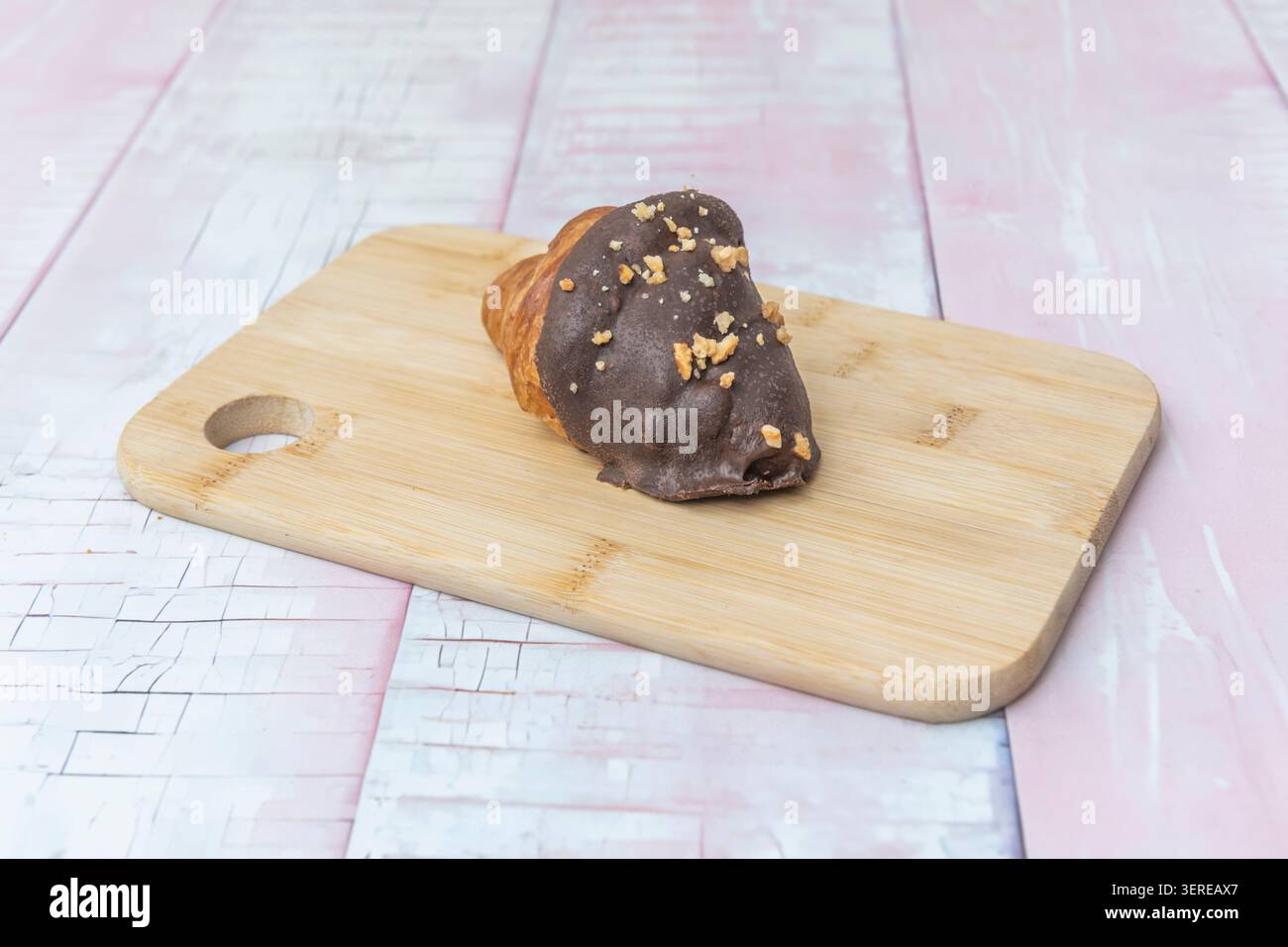 A chocolate-glazed croissant topped with chopped nuts sits on a bamboo ...