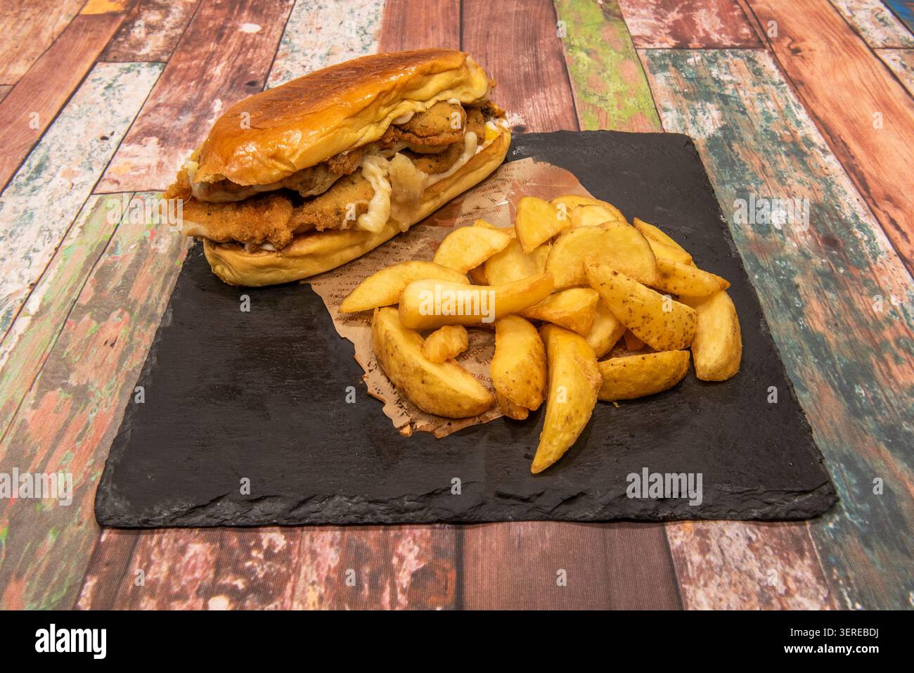 Crispy chicken bocadillo with melted cheese and a side of potato wedges ...