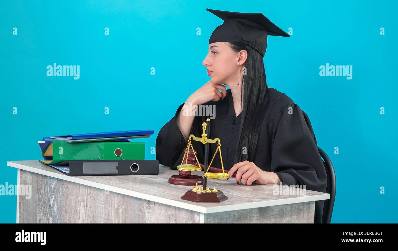 Woman in graduation cap at desk on blue background Stock Photo - Alamy