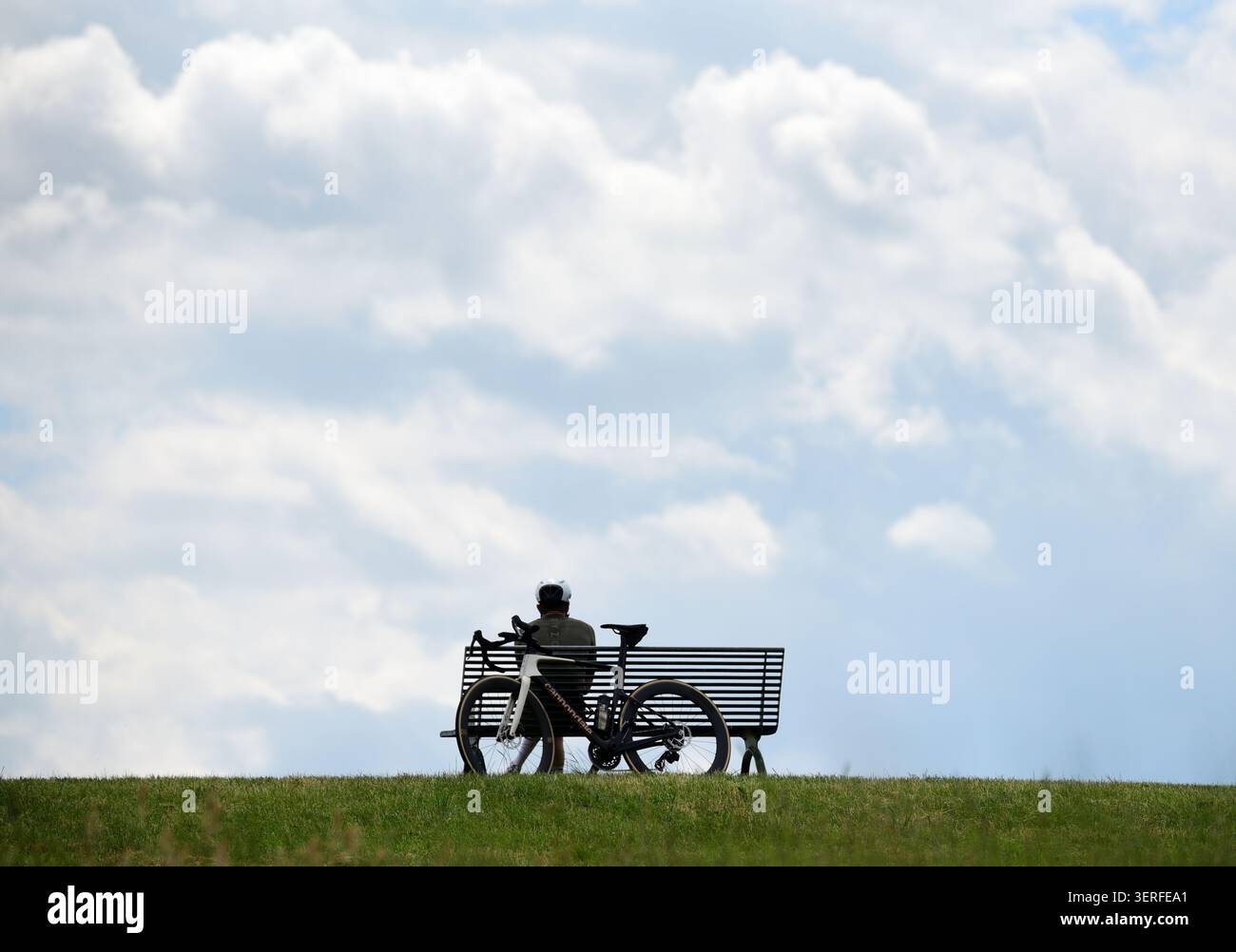 Hamburg, Germany. 18th Jun, 2026. A road cyclist is sitting on a bench ...