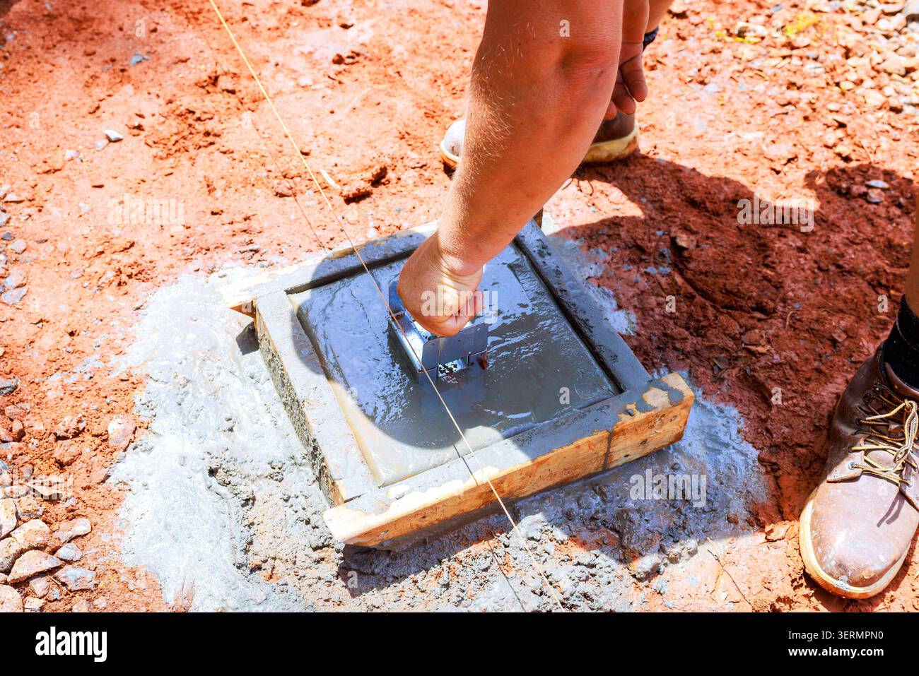 Worker install anchor bracket mixes levels cement in wooden frame at ...