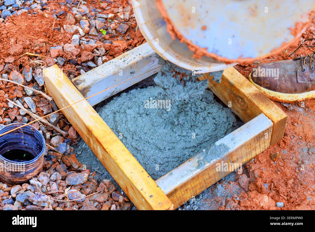 Worker pours concrete from container into wooden mold at construction ...