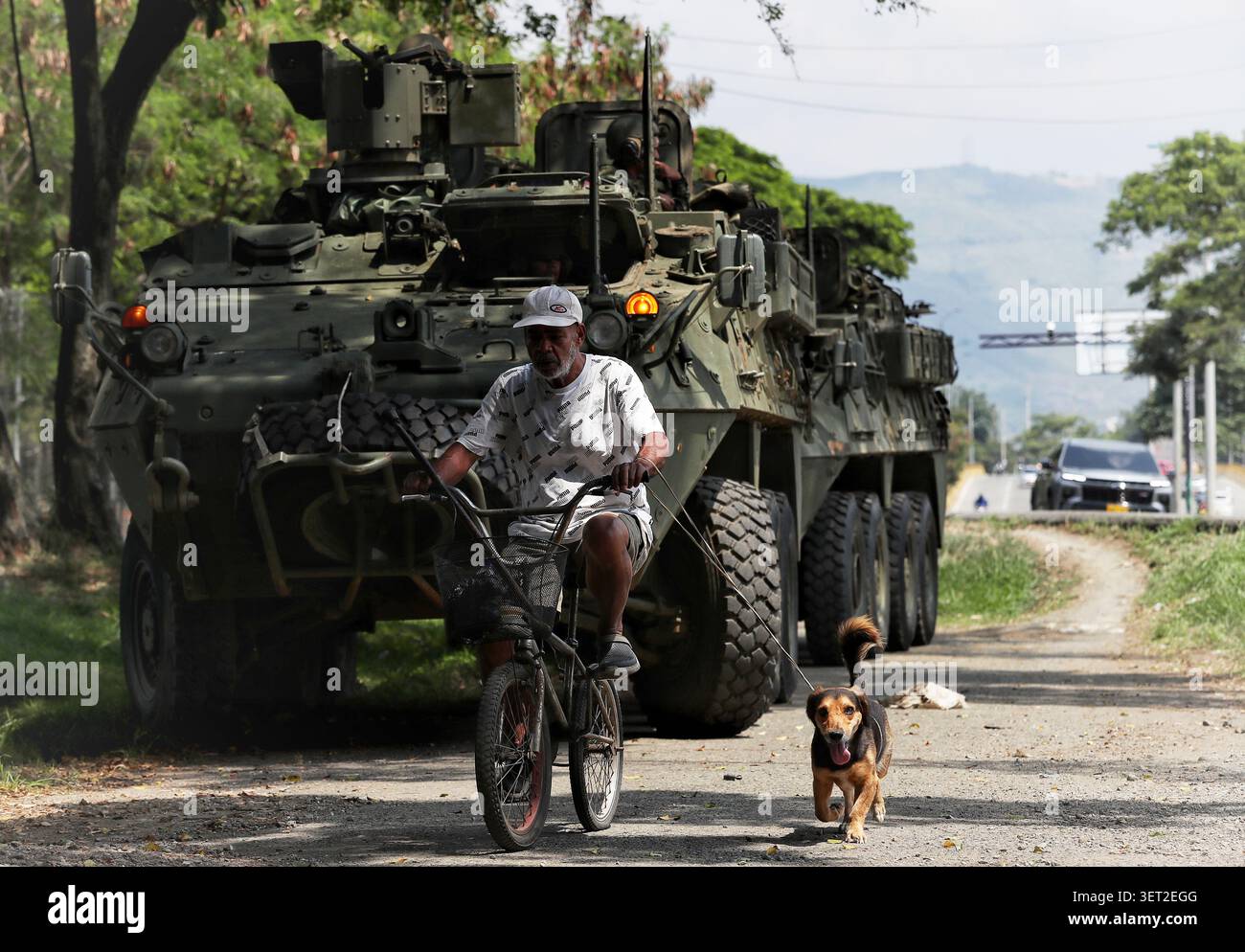 A man bicycles with his dog past army armored vehicles in Cali ...