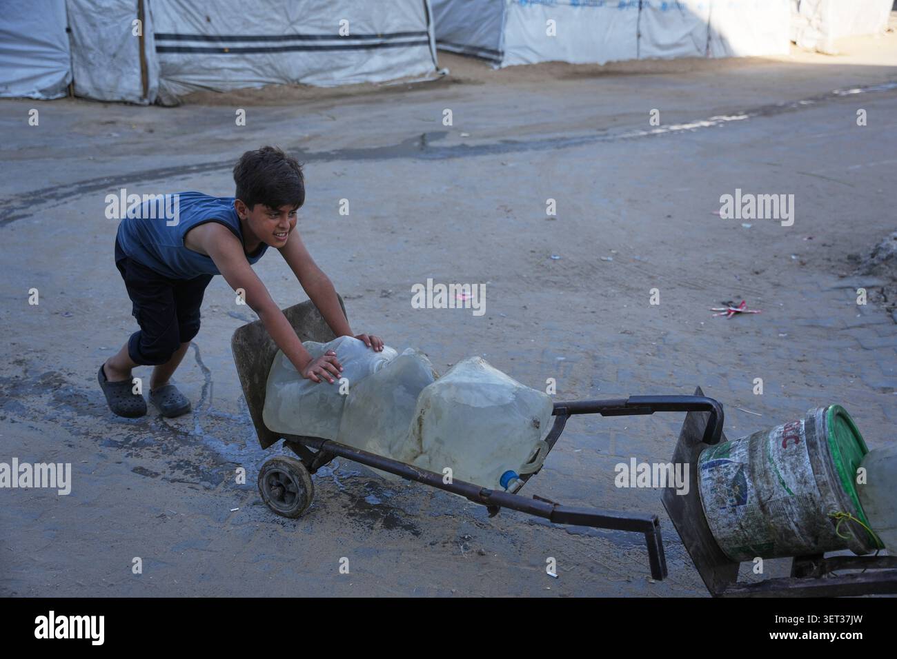 A displaced Palestinian boy hauls water containers at the Yarmouk ...
