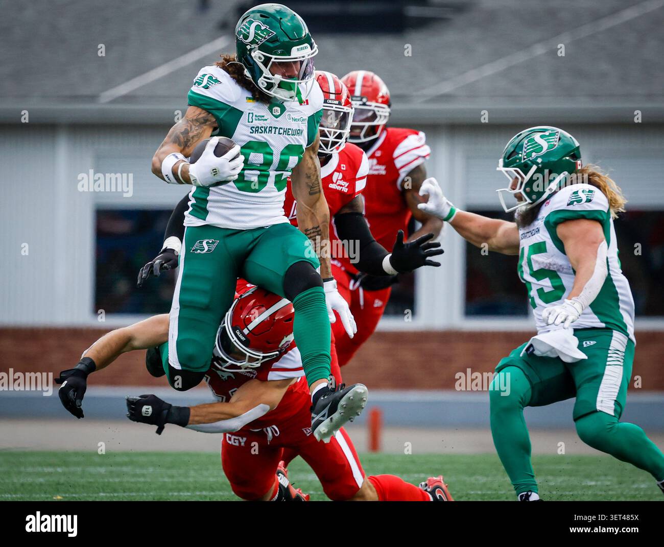 Saskatchewan Roughriders' Kian Schaffer-Baker, left, leaps over Calgary ...