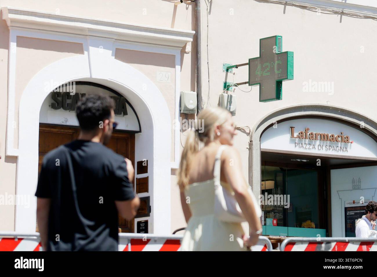 People walk past a pharmacy whose thermometer reports 42 Celsius ...