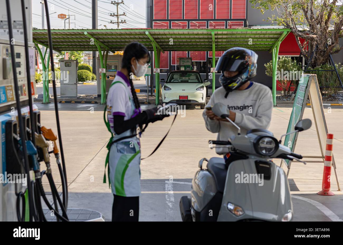 A motorcyclist fills his tank in front of an electric vehicle charging ...