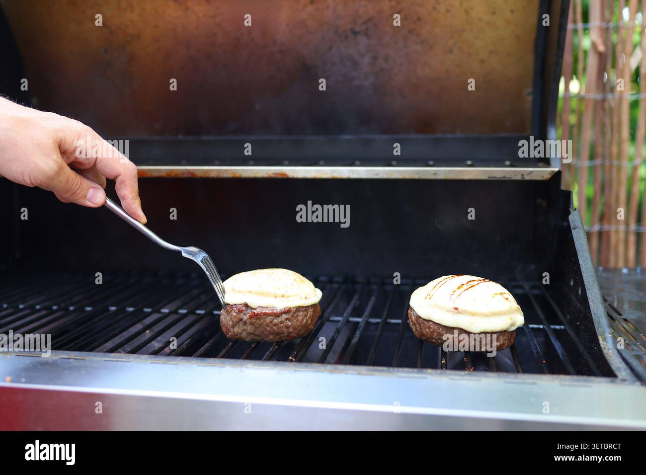 Grilling juicy beef patties topped with melted cheese on a barbecue ...