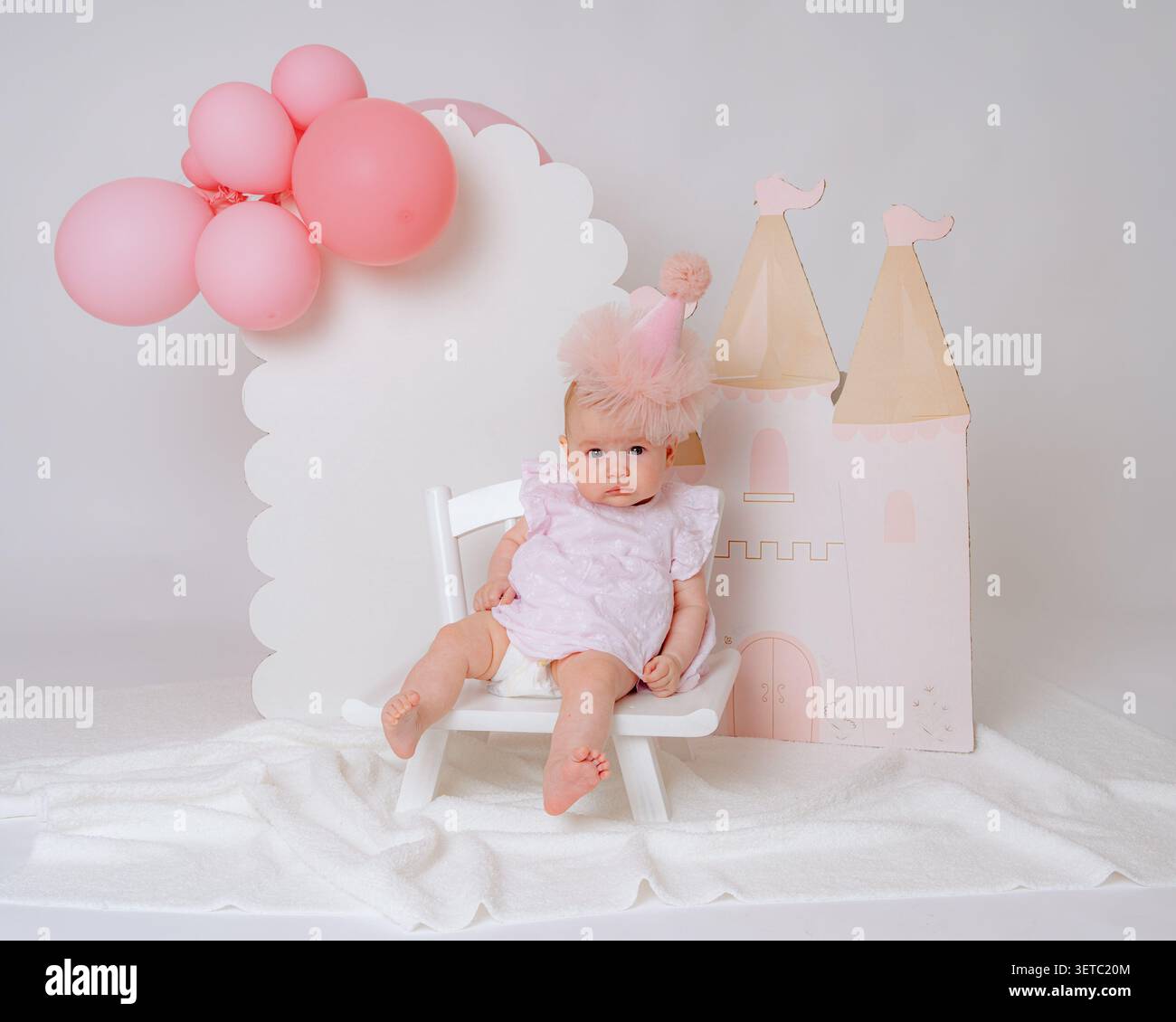 Adorable six month old baby girl sitting on a small white chair with ...