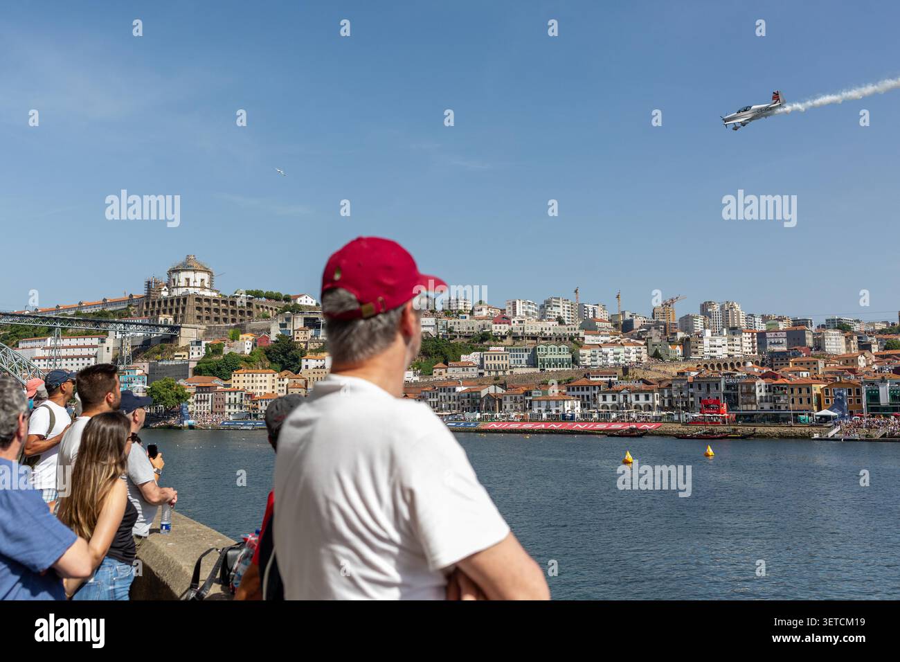 Spectators stand along the riverside promenade as an aerobatic aircraft ...