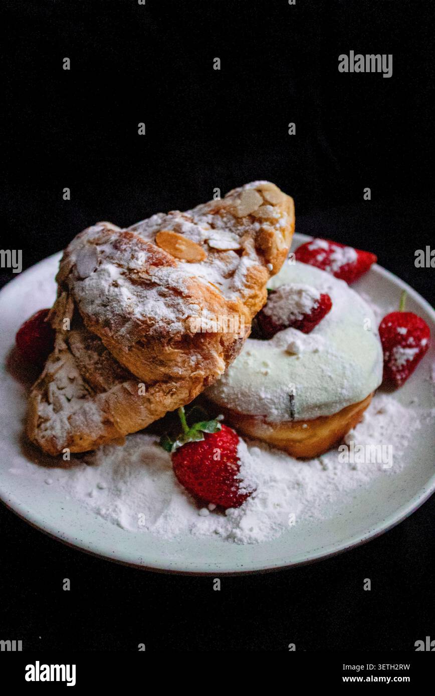 Croissant and donut with sugar powder alongside with some strawberries ...