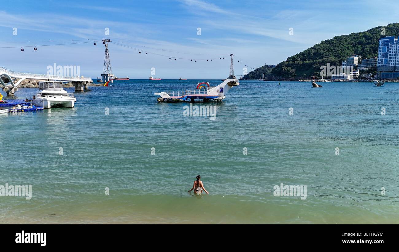 Woman wading in the aqua waters of songdo beach with cable car cabins ...