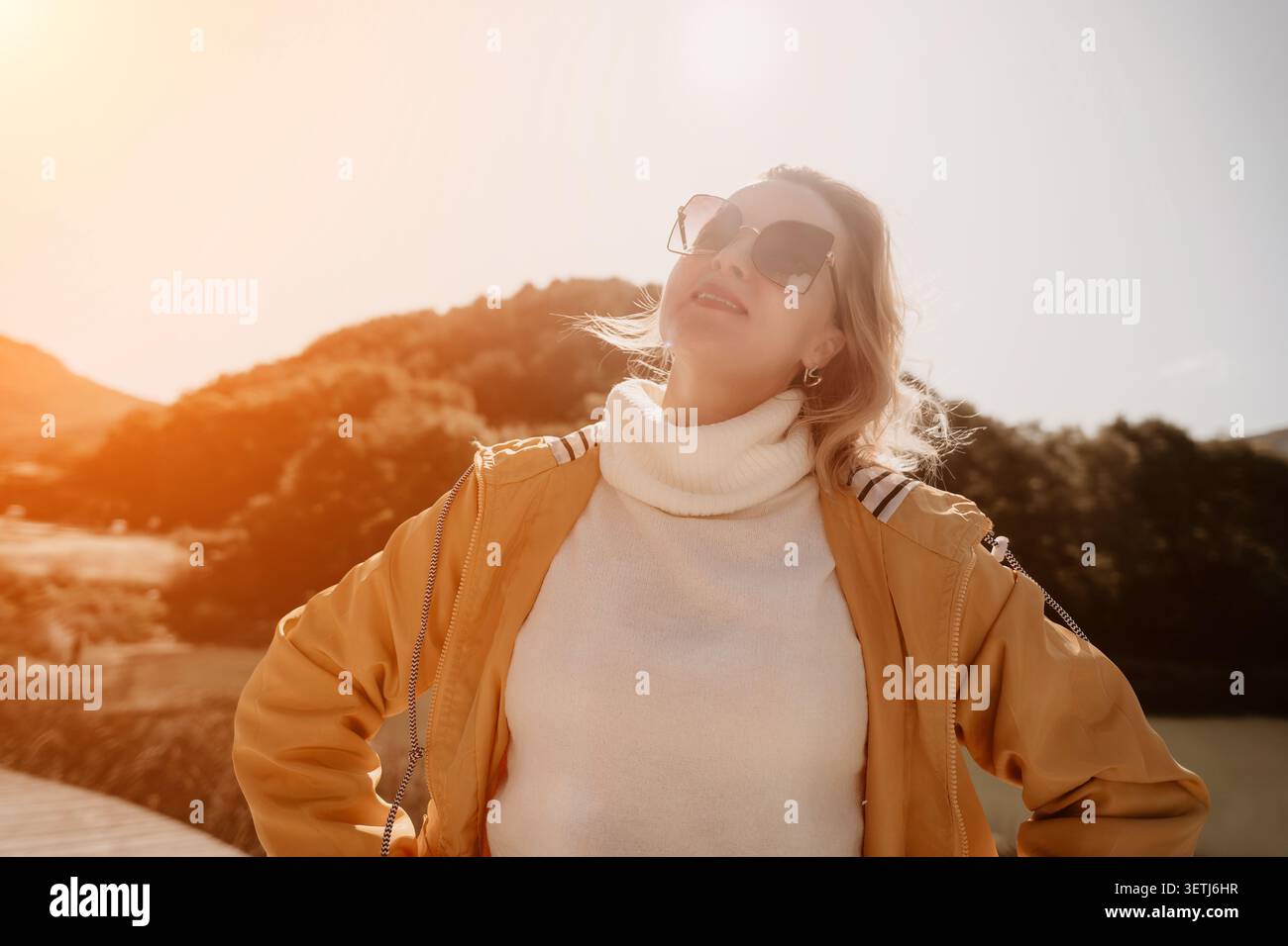 A woman wearing a yellow jacket and sunglasses stands against a ...
