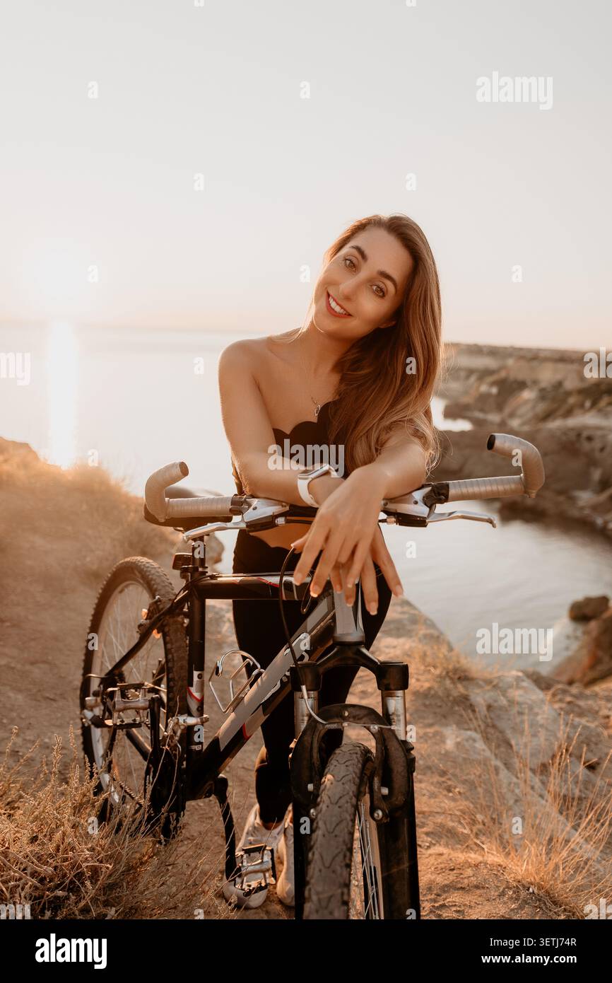 A young woman with long brown hair leans on a mountain bike on a rocky ...