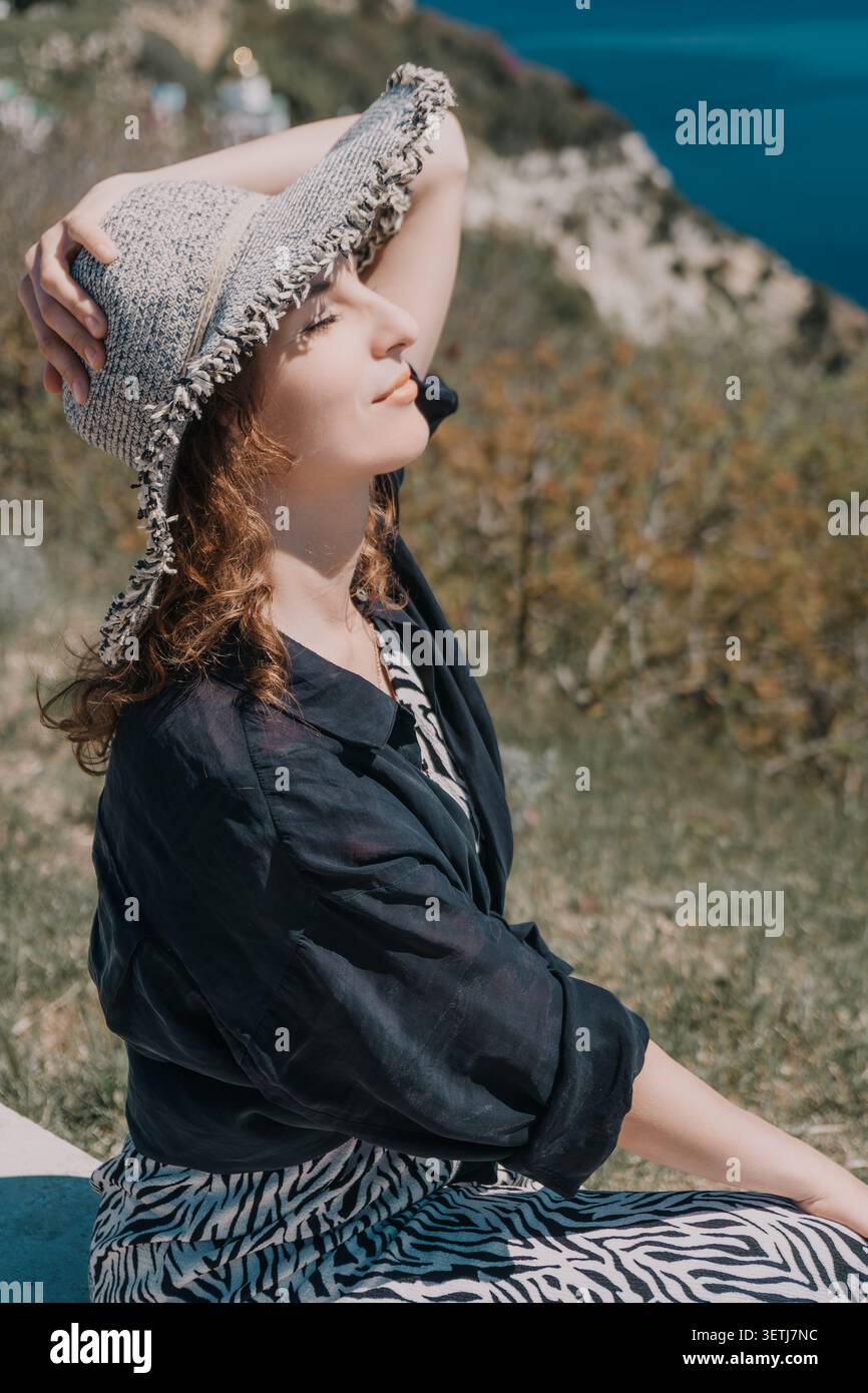 Young woman wearing a straw hat and black clothing resting in a sunlit ...