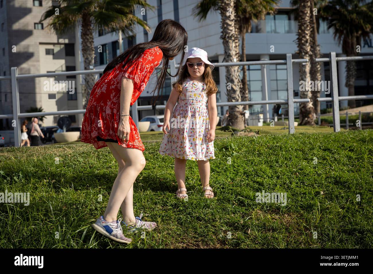 A mother bent down towards her little daughter while walking on a green ...