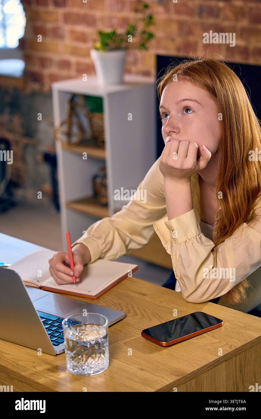 Thoughtful teenage girl writing notebook beside laptop at home Stock ...