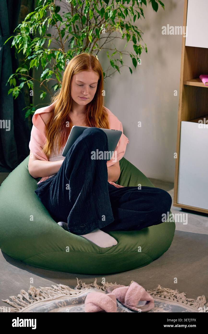 Teenage girl reading tablet on green beanbag at home Stock Photo - Alamy