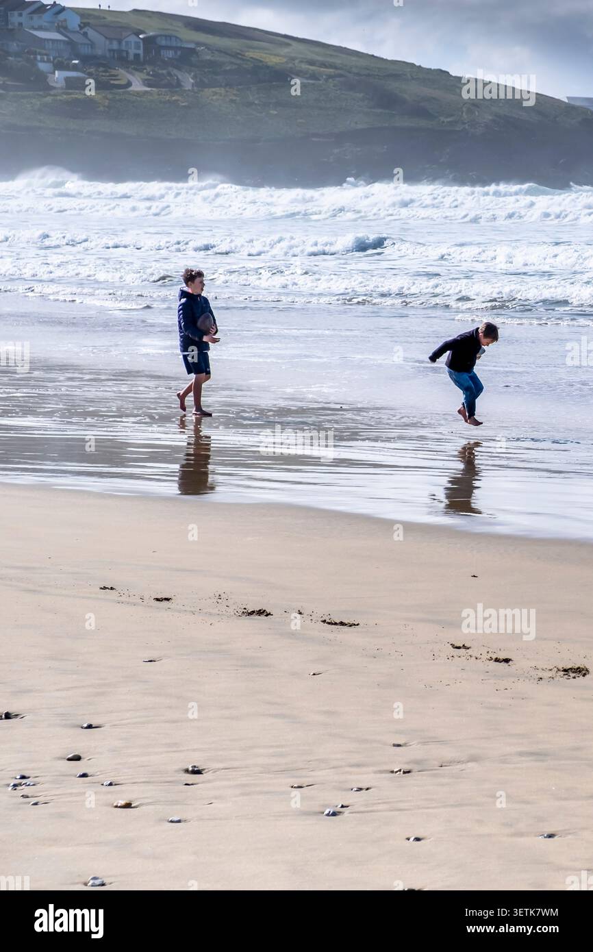 Two young boys walking barefoot on Fistral Beach on the coast of ...