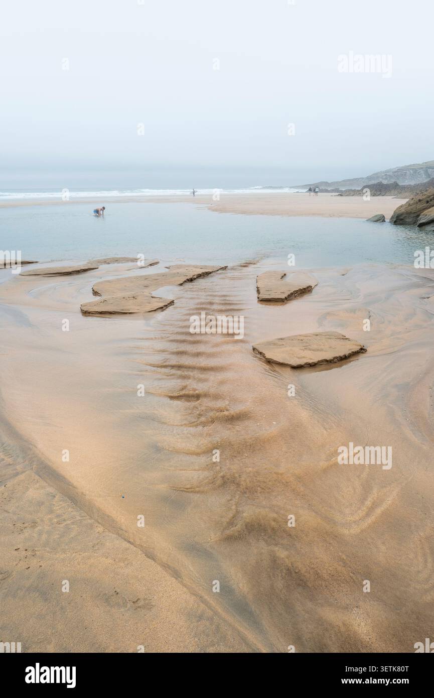Water flowing across Fistral Beach at low tide on a misty foggy day on ...