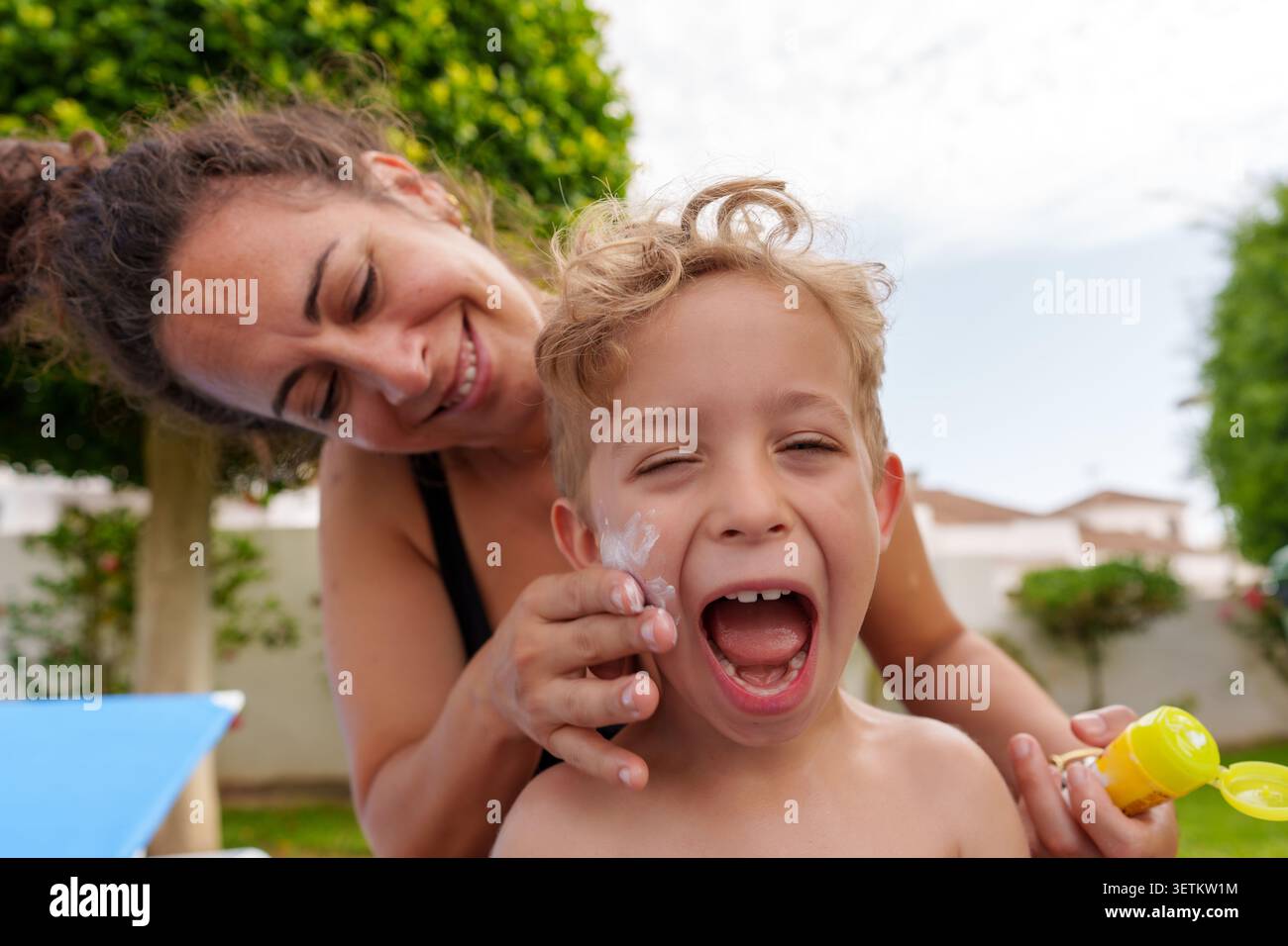 Happy mother applying protective sunscreen lotion to her son's face ...