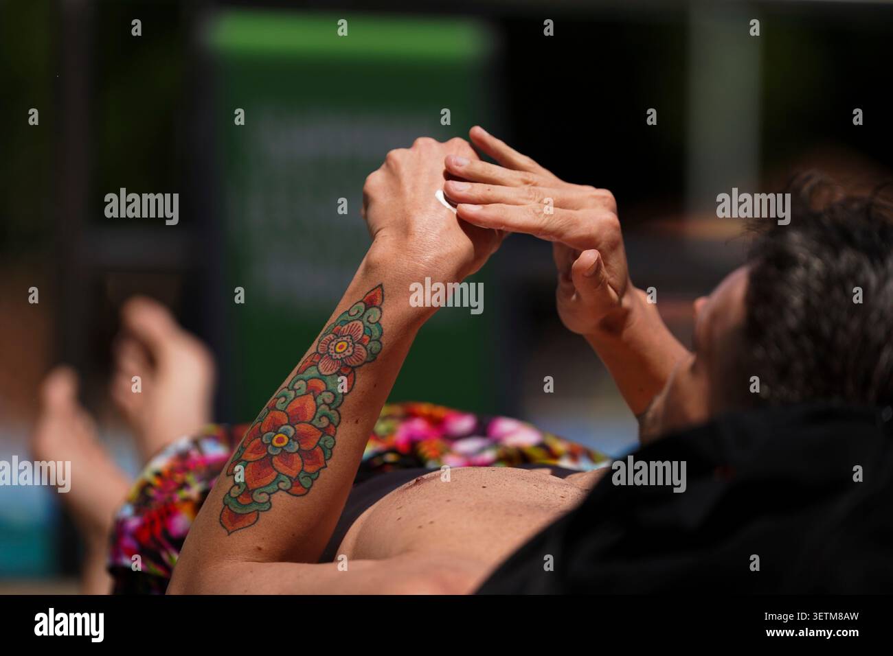 A man spreads sun cream at a swimming pool in London, Tuesday, June 23 ...
