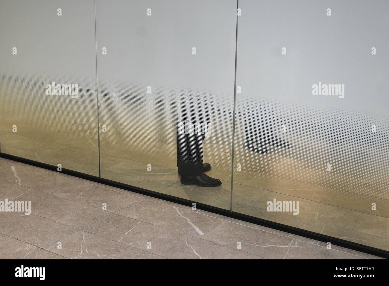 The feet of office workers are seen behind a glass barrier inside an ...