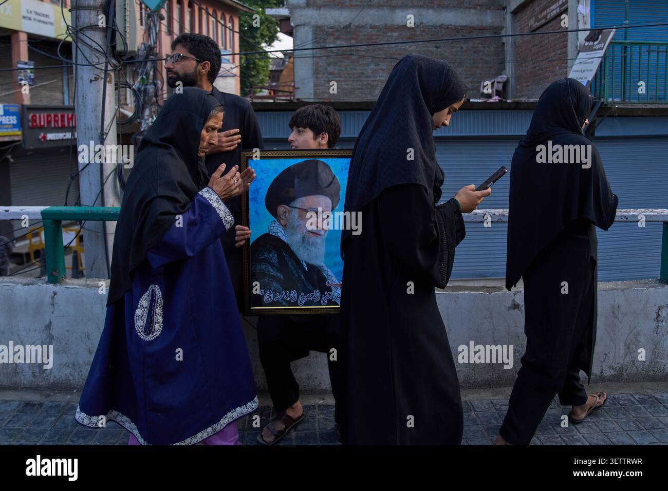 Kashmiri Shiite Muslim women walk past a boy holding a photograph of ...