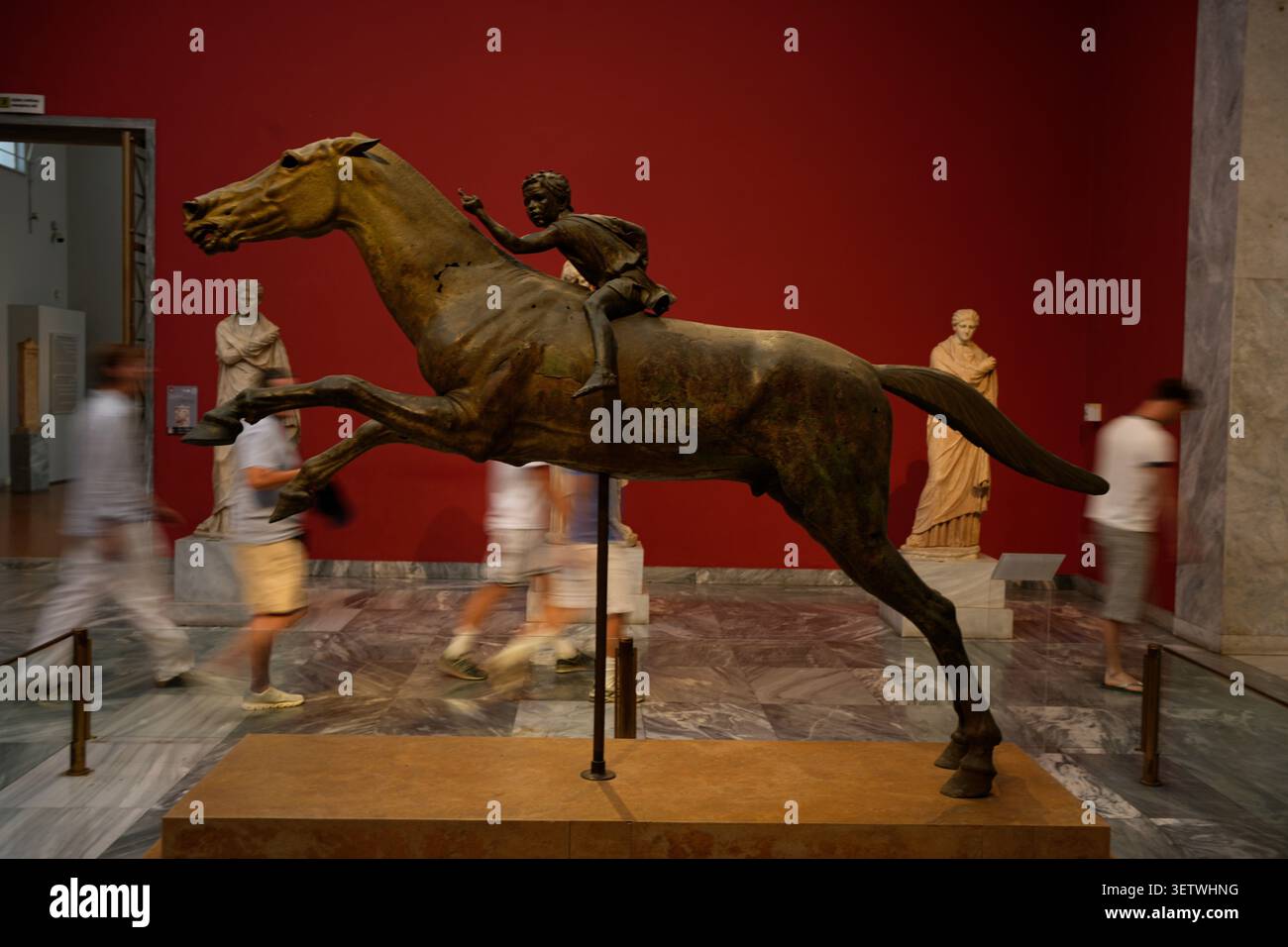 Tourists pass next to the bronze statue of a young jockey riding a ...