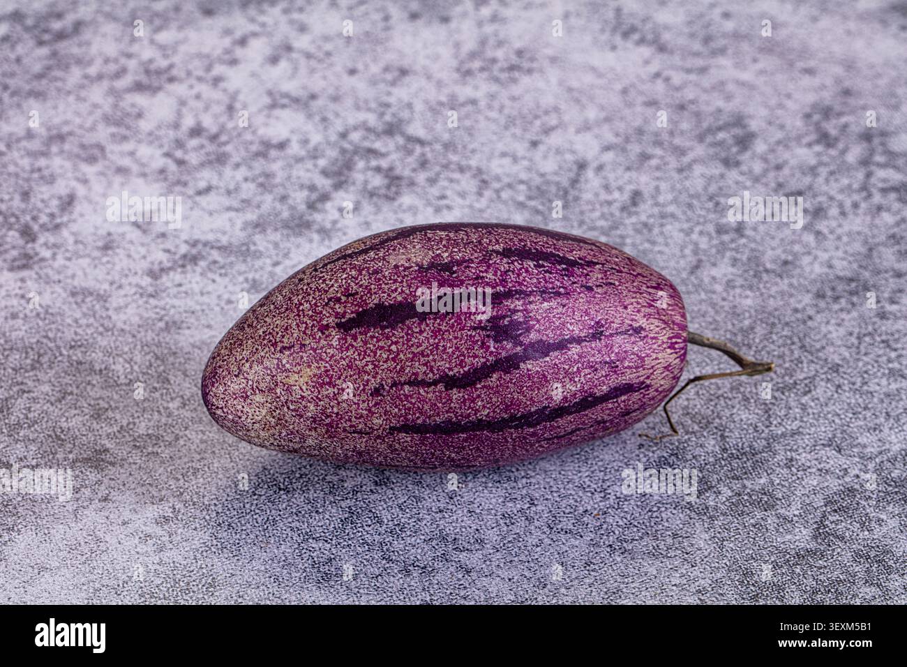 Single purple fruit with dark stripes speckled skin rests on textured ...