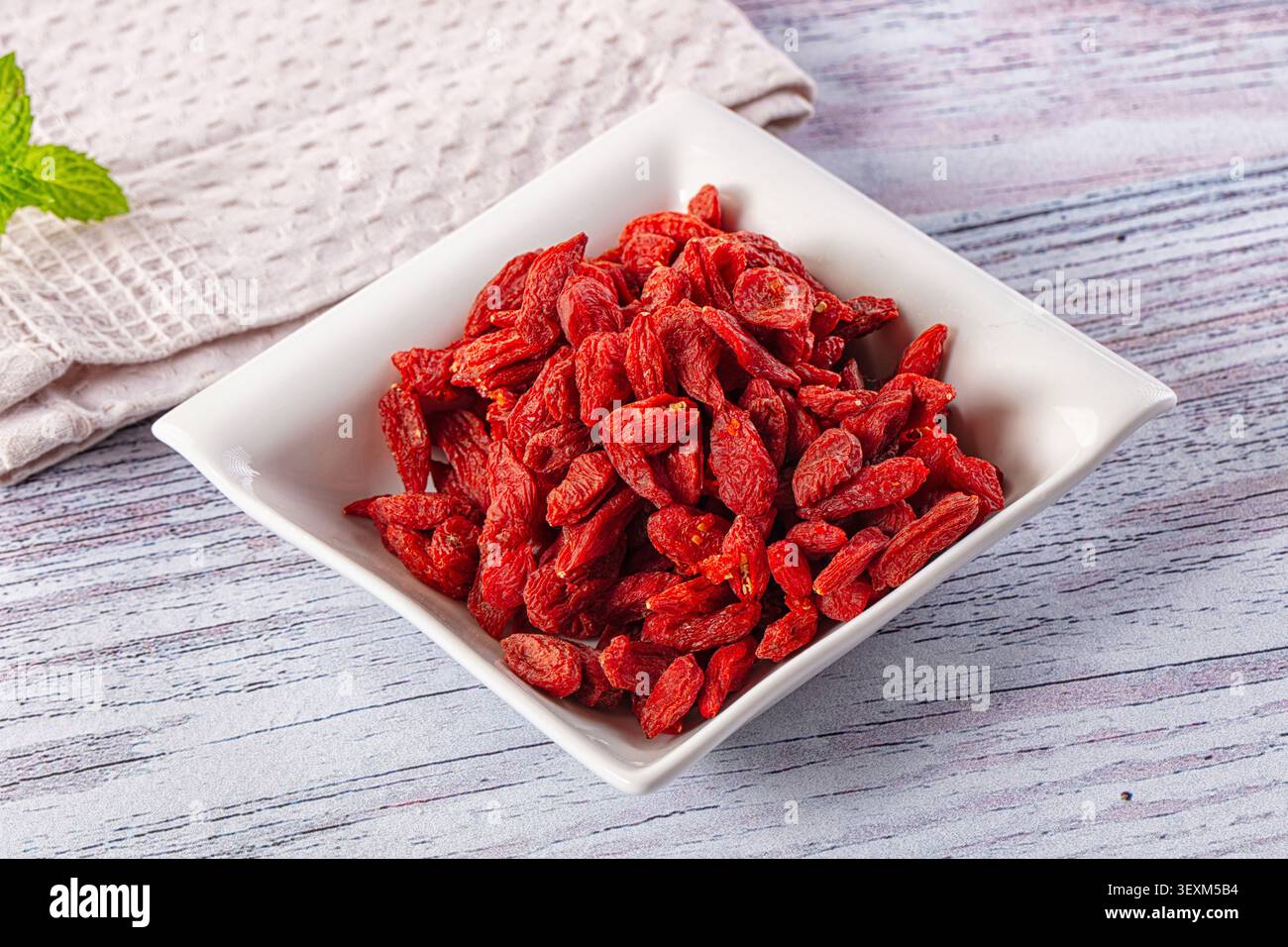 Vibrant red goji berries fill white square bowl on weathered wood table ...